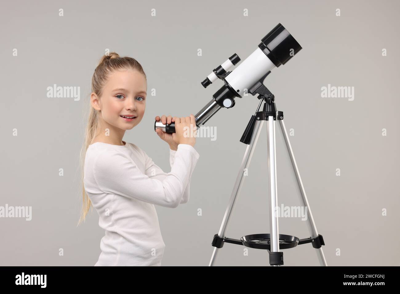 Happy little girl with telescope on light grey background Stock Photo ...