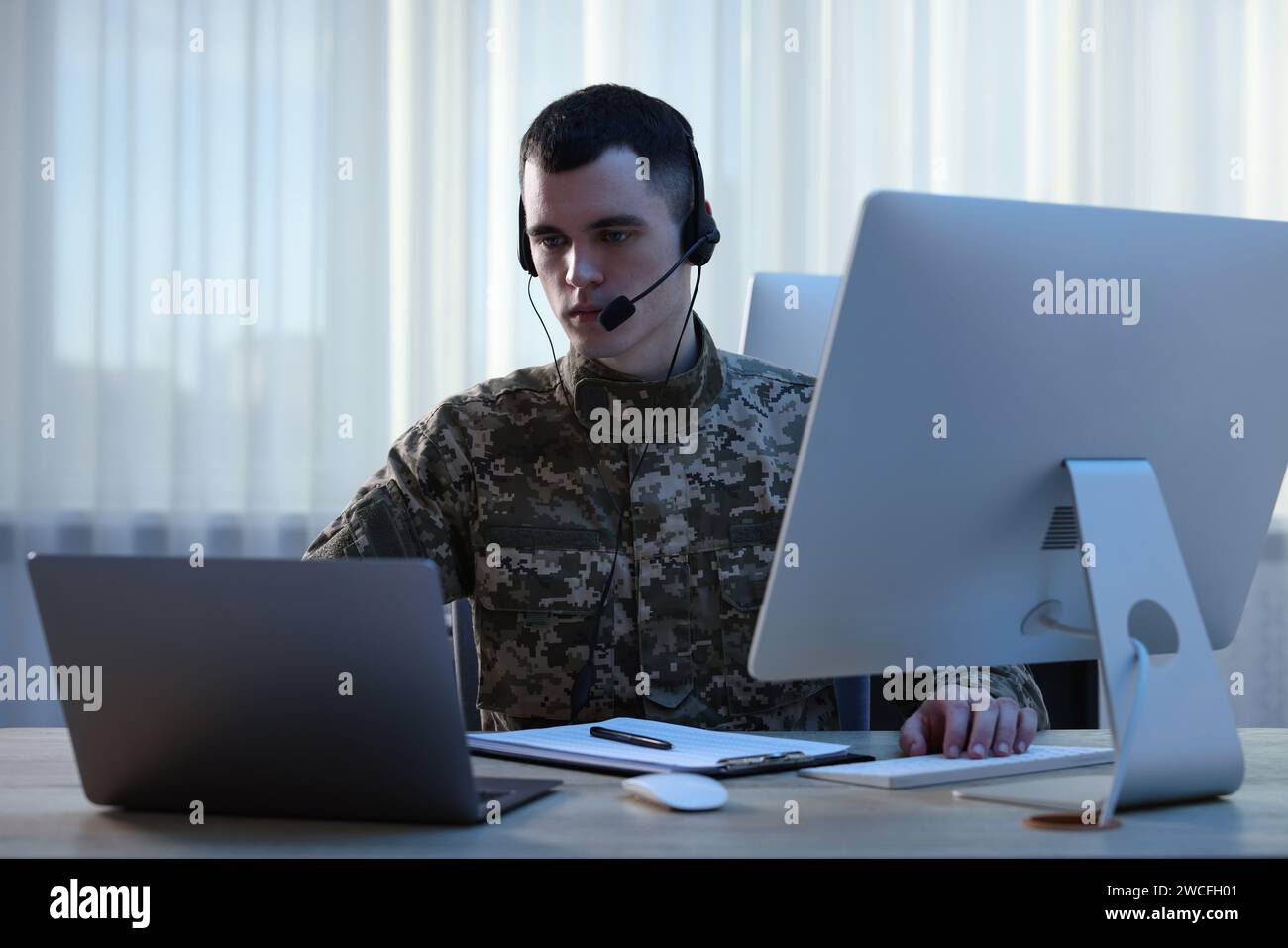Military service. Young soldier in headphones working at wooden table ...