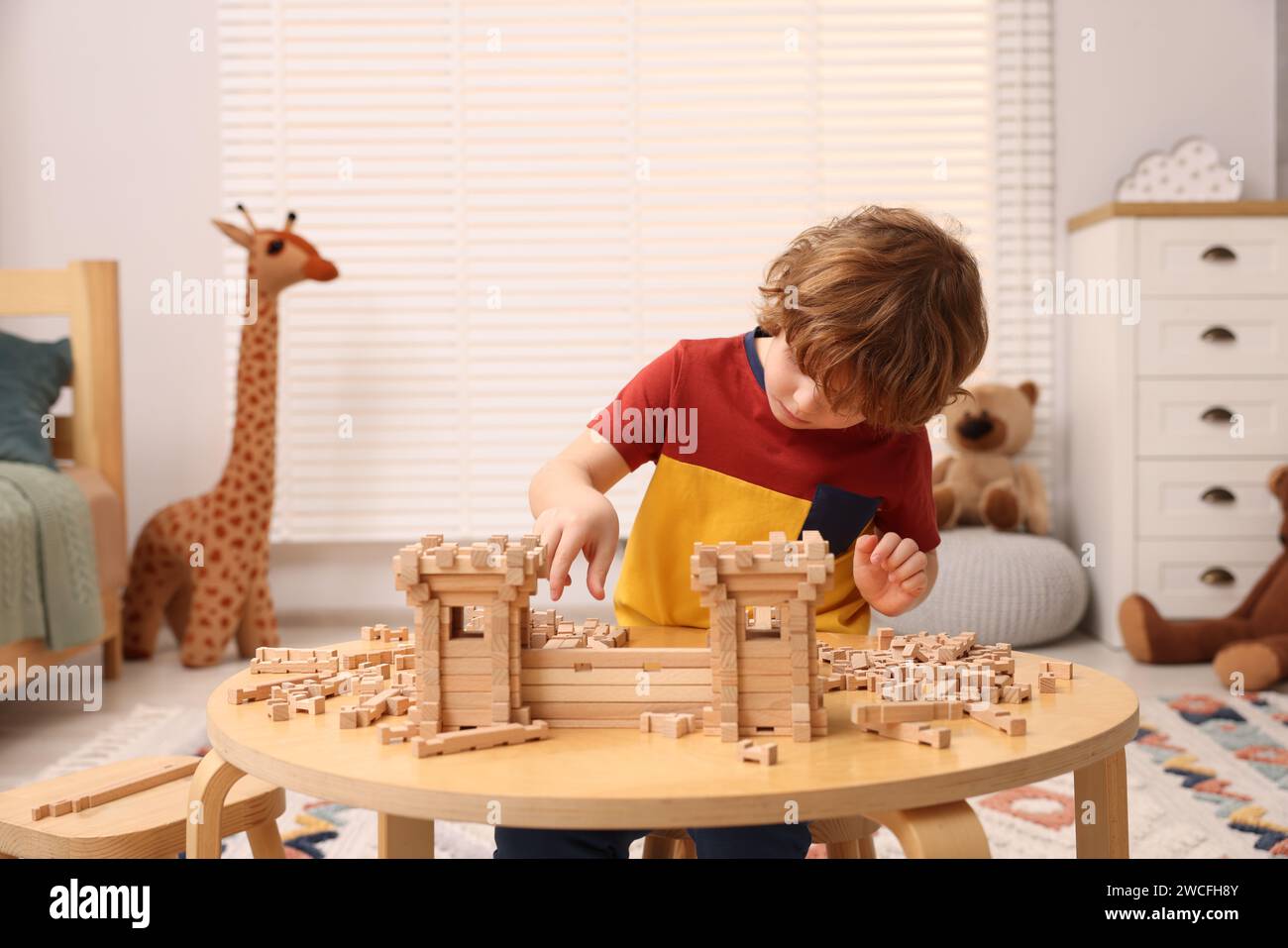 Little boy playing with wooden entry gate at table in room. Child's toy ...