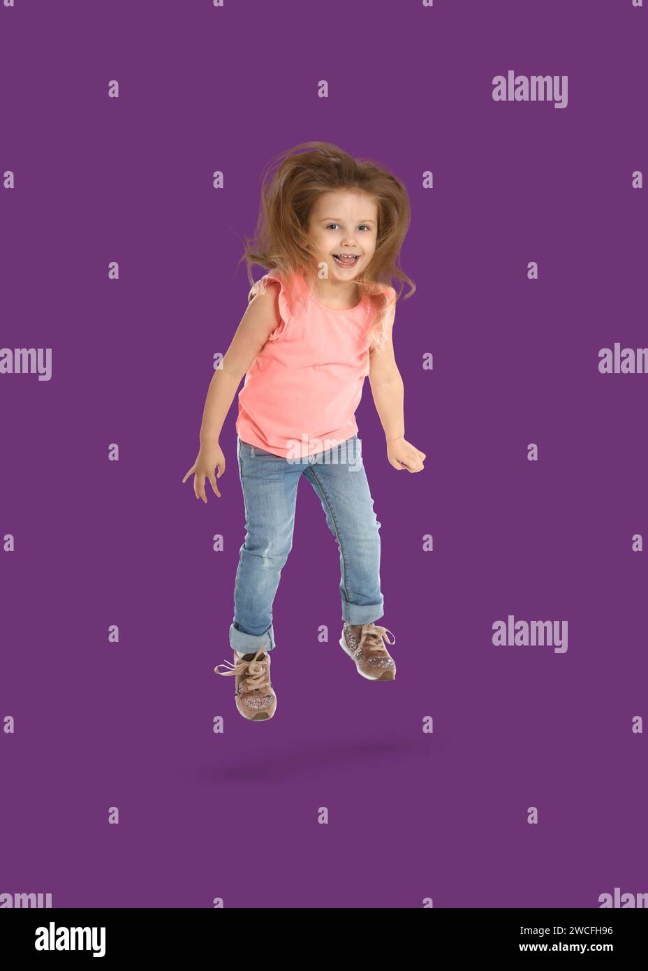 Happy cute girl jumping on purple background Stock Photo - Alamy