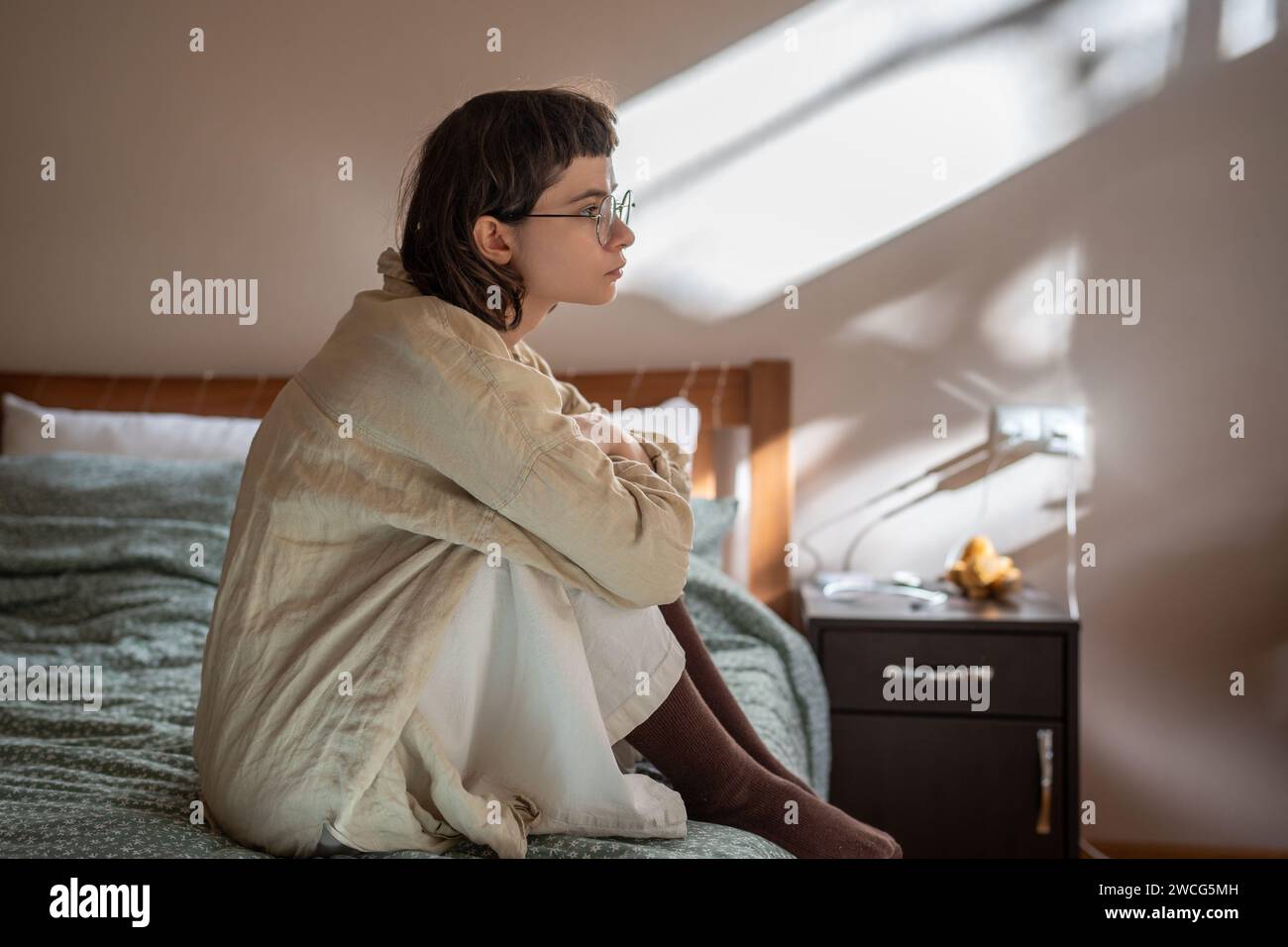 Depressed tired teenage girl sitting on bed sadly looking at window ...