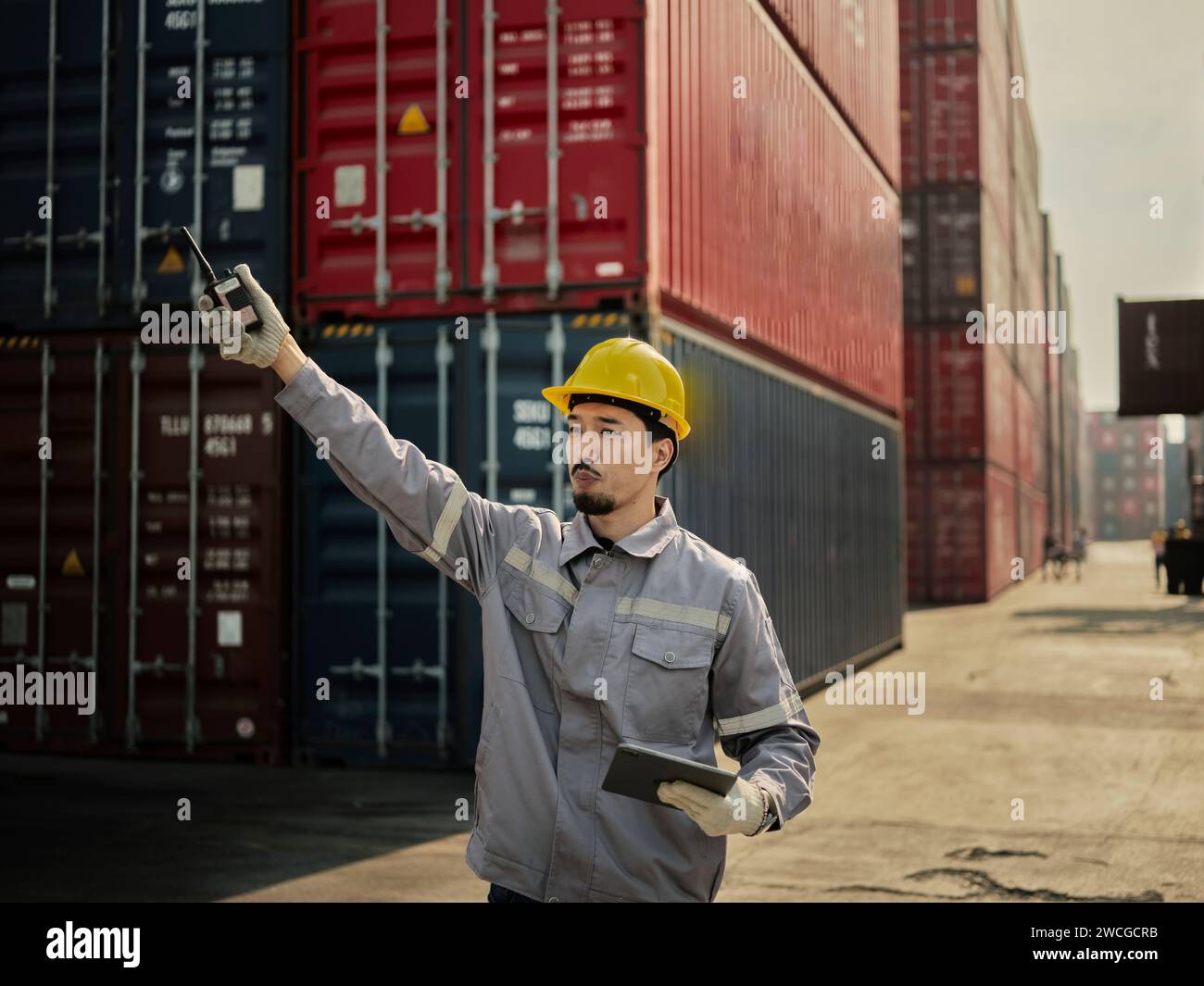 Asian worker wearing safety helmet and using walkie talkie in front of ...