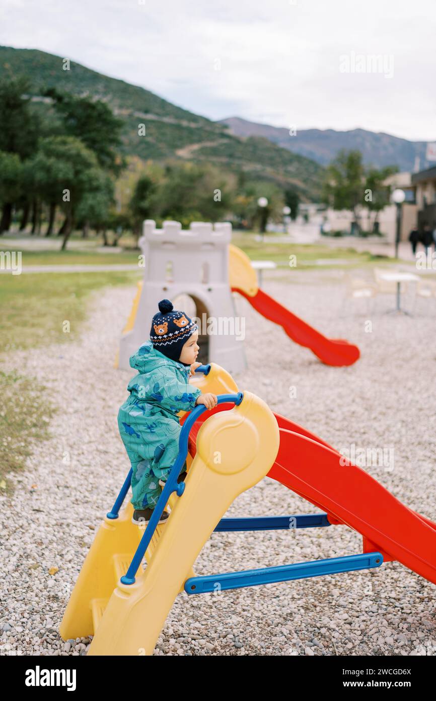 Little girl climbs the stairs to the colorful slide in the playground ...