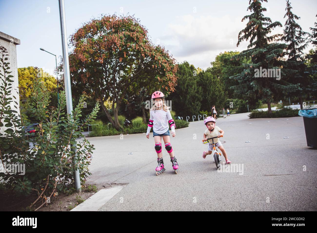 Two little girls rides on rollers and runbike in summer park. Children ...