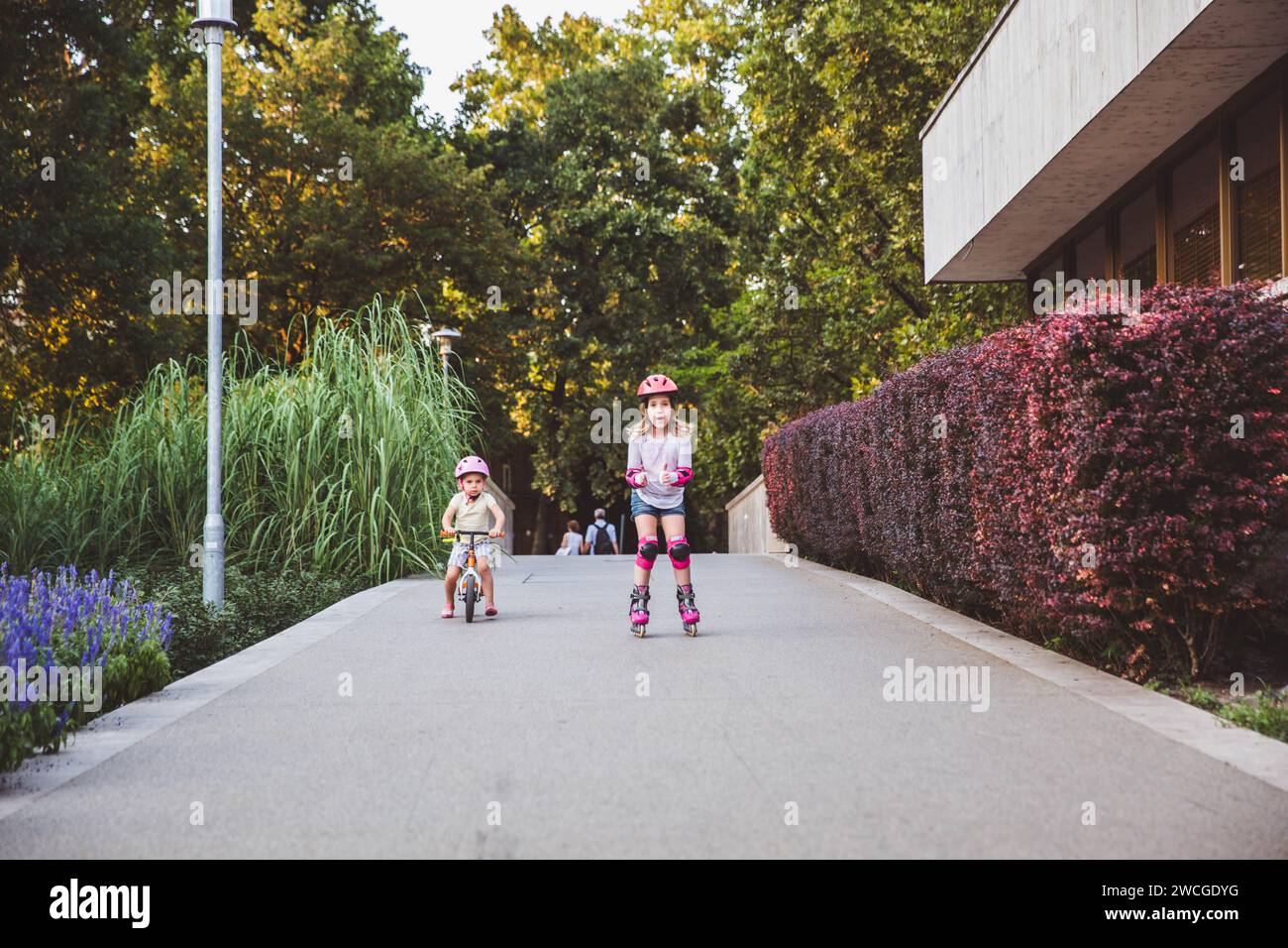 Two little girls rides on rollers and runbike in summer park. Children ...