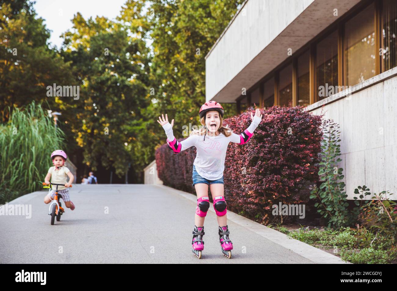 Two little girls rides on rollers and runbike in summer park. Children ...