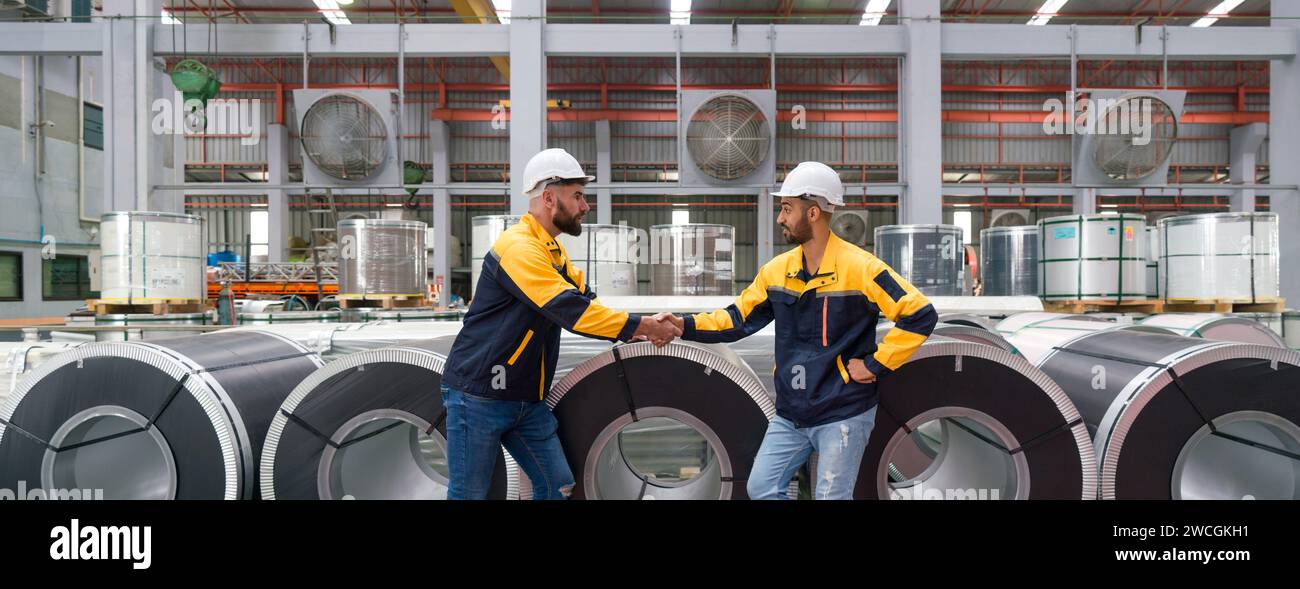 Two people shaking hands in front of large rolls of steel at an ...