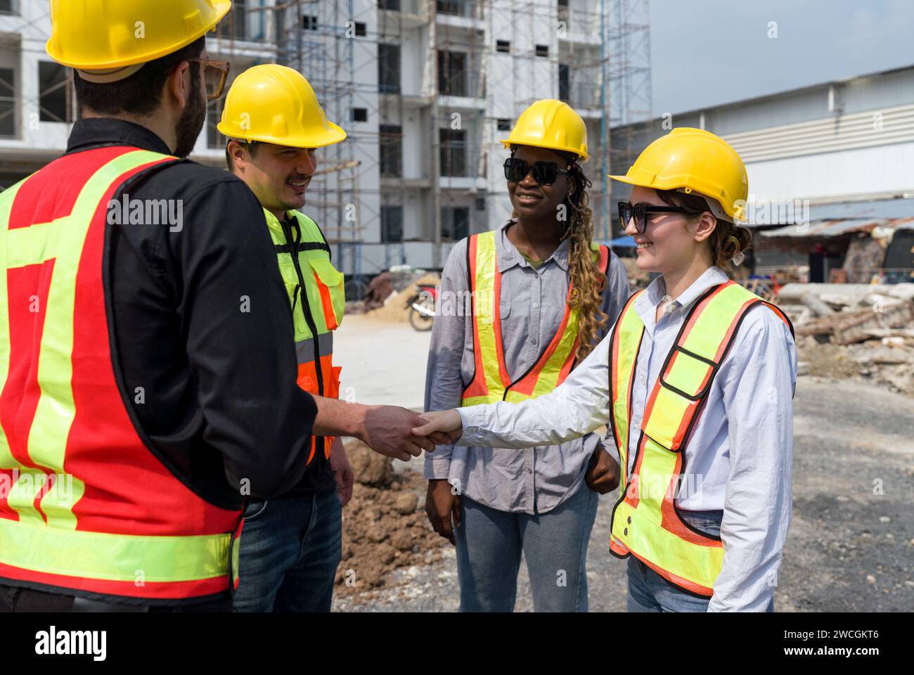 Four construction workers celebrating with a handshake in front of an ...
