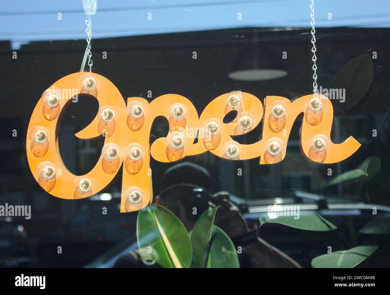 An open sign displayed on window side amidst lush green plants Stock ...