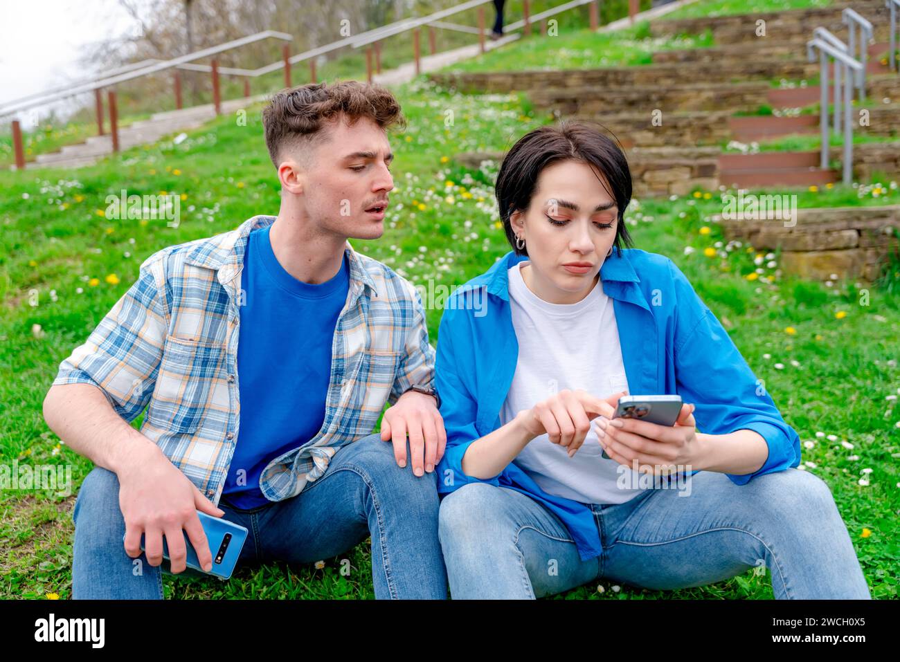 Sad couple using phones outdoors. A man peeping into a woman's phone ...