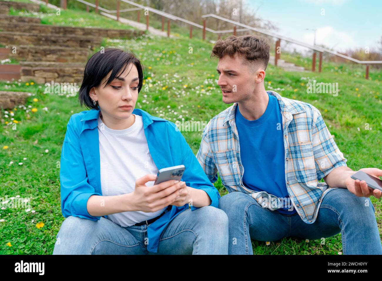 Sad couple using phones outdoors. A man peeping into a woman's phone ...