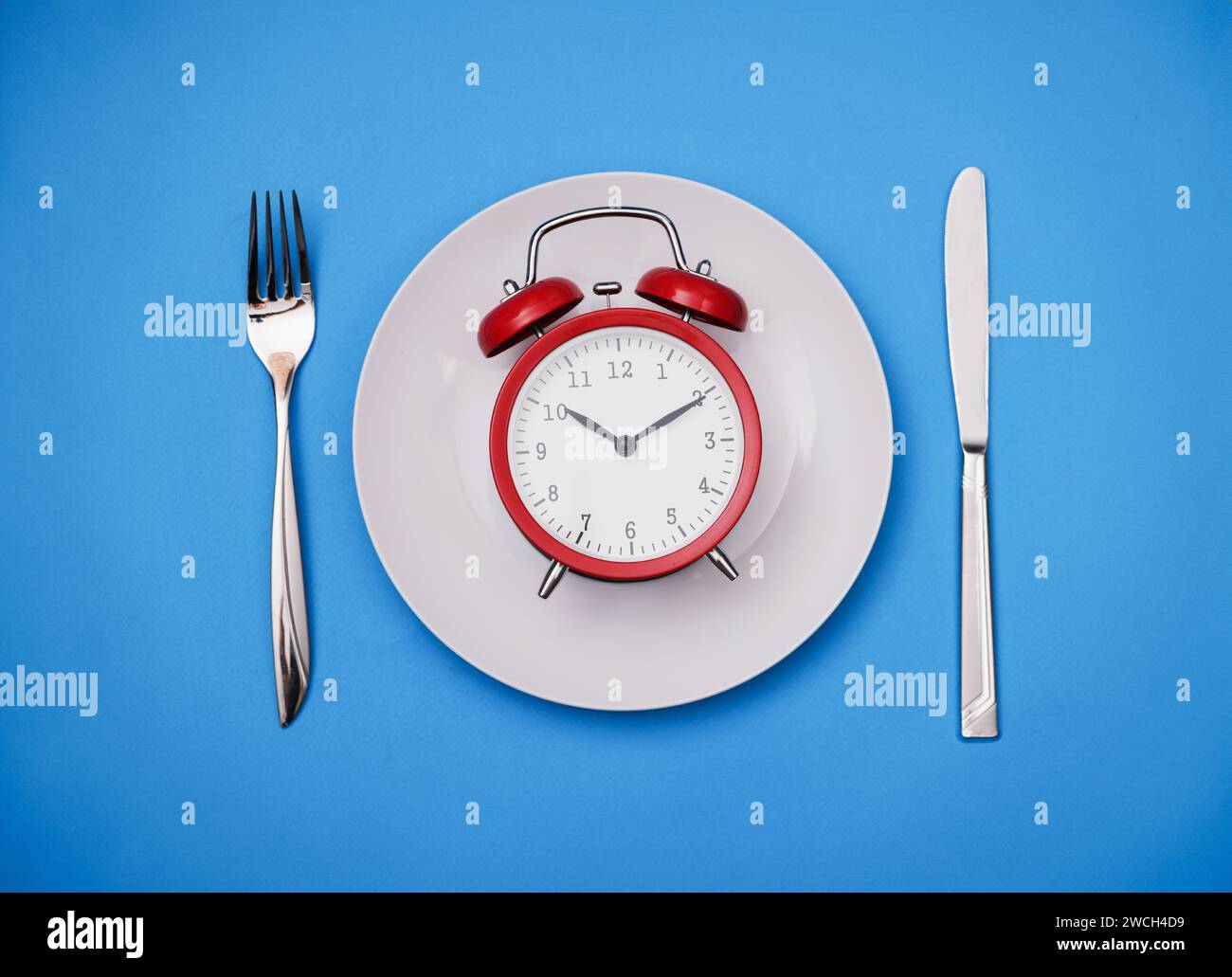 Red alarm clock lies on plate next to fork and knife Stock Photo - Alamy