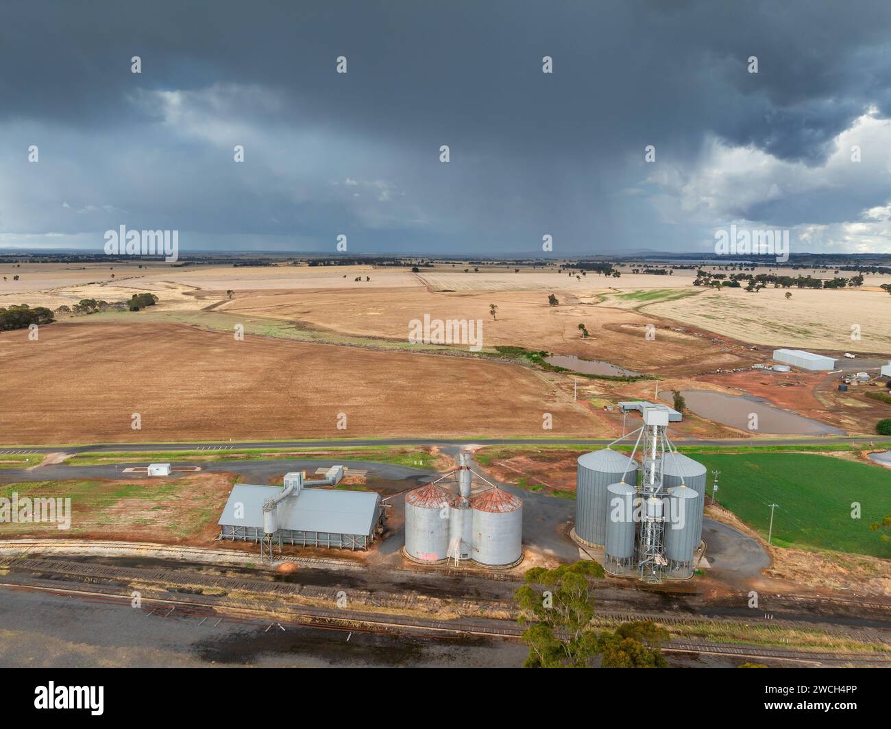 Aerial view of grain silos along a rural railway line with dark clouds ...