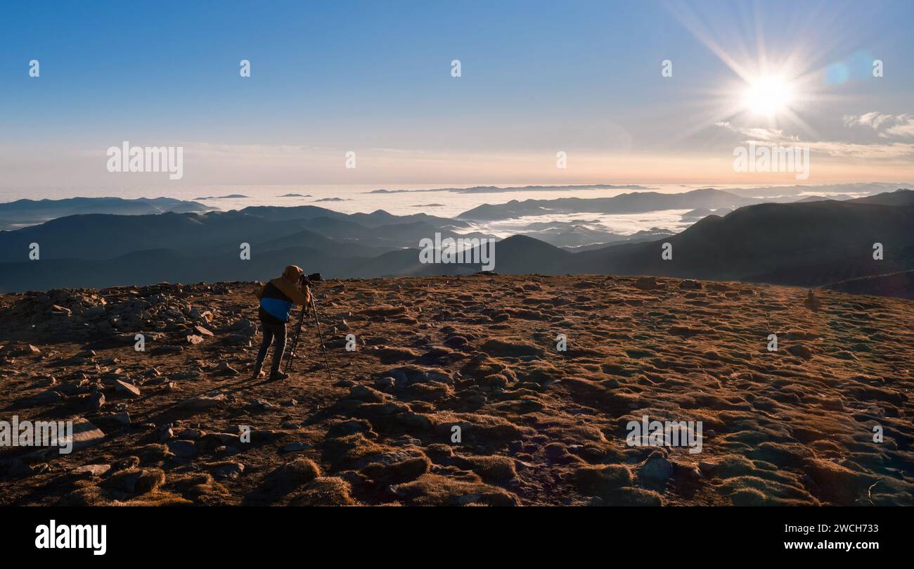 Hiker at the mountain peak with a camera on a tripod photographs ...