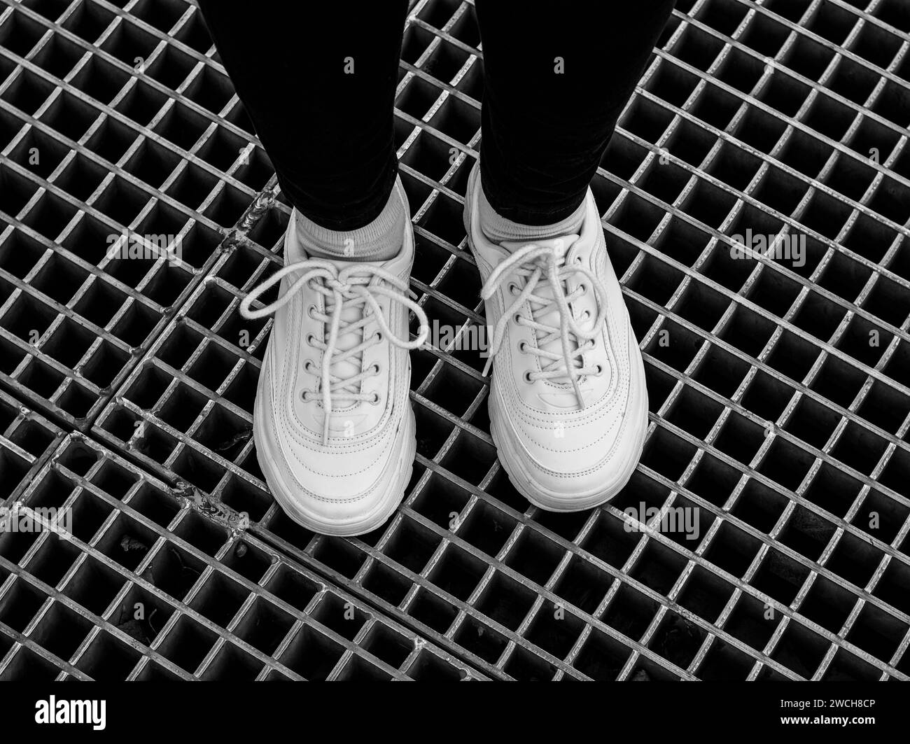 Foot standing. The girl in white sneakers is on a metal grid. View from ...