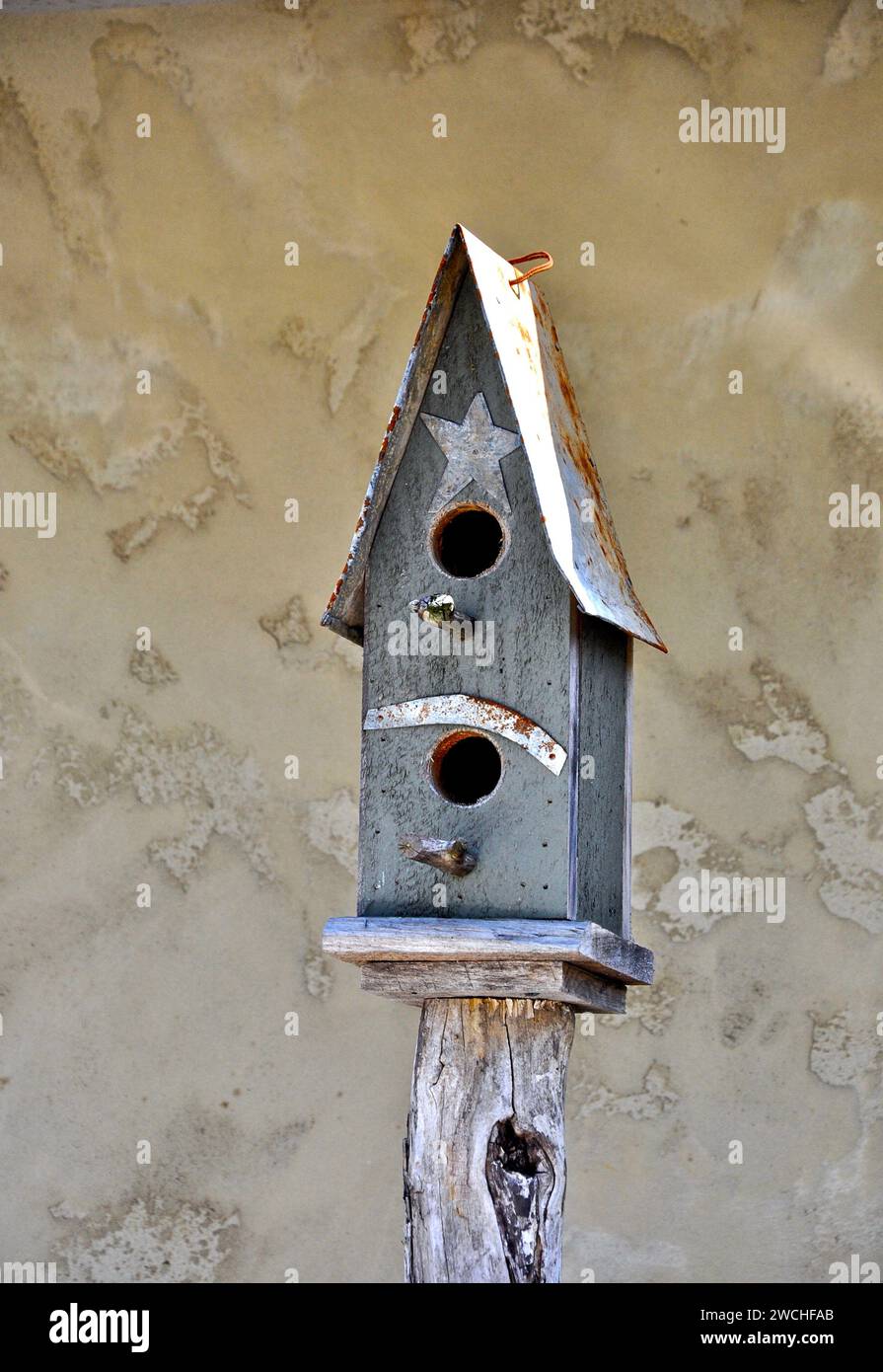 A charming wooden birdhouse perched atop a sturdy pole against a wall ...