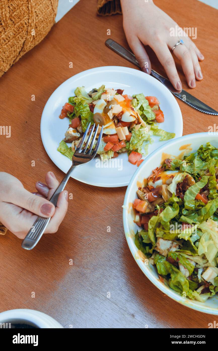 vertical image of unrecognizable woman sitting eating salad with fork ...