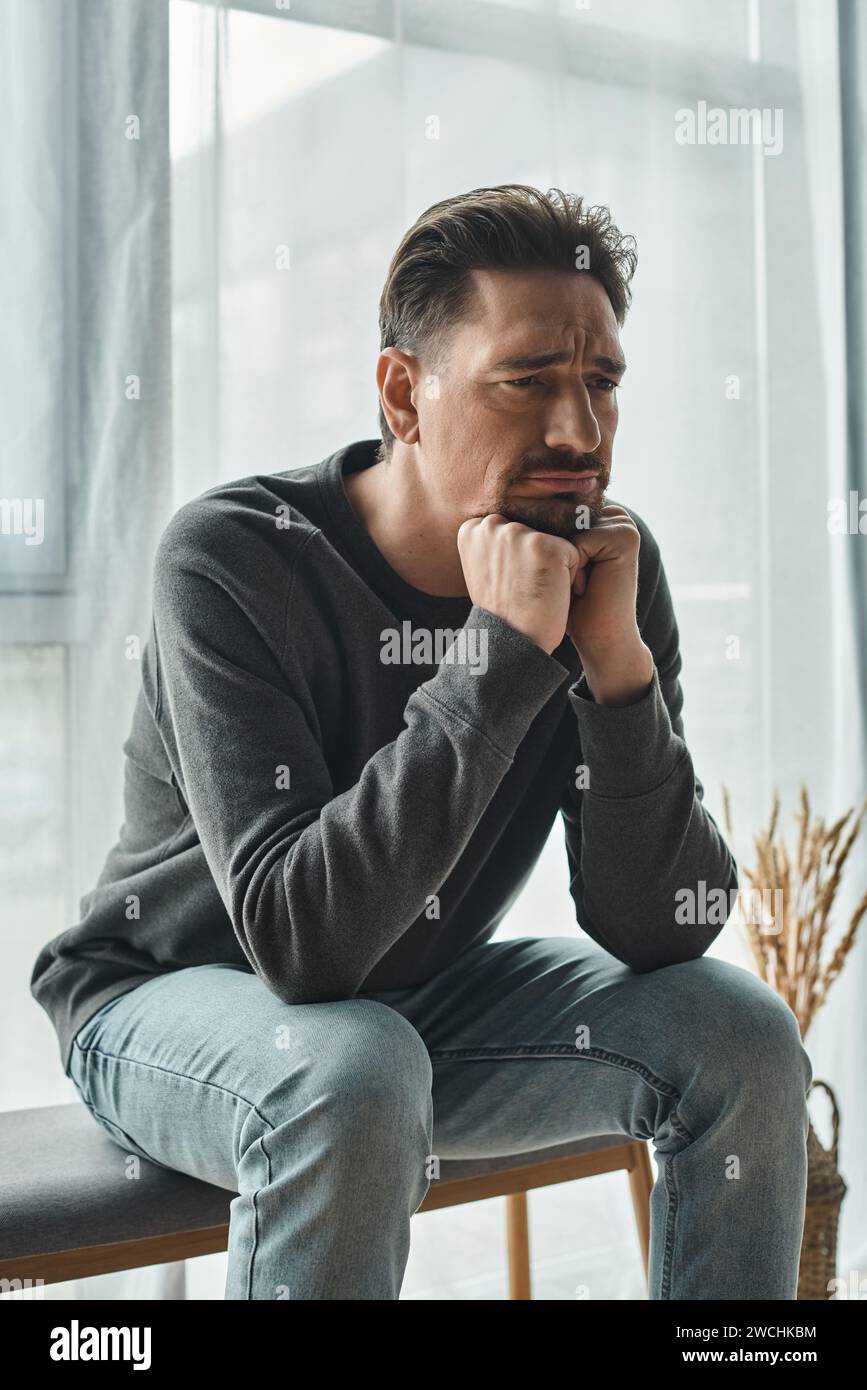 sad and bearded man in casual home wear sitting on bedroom bench and ...