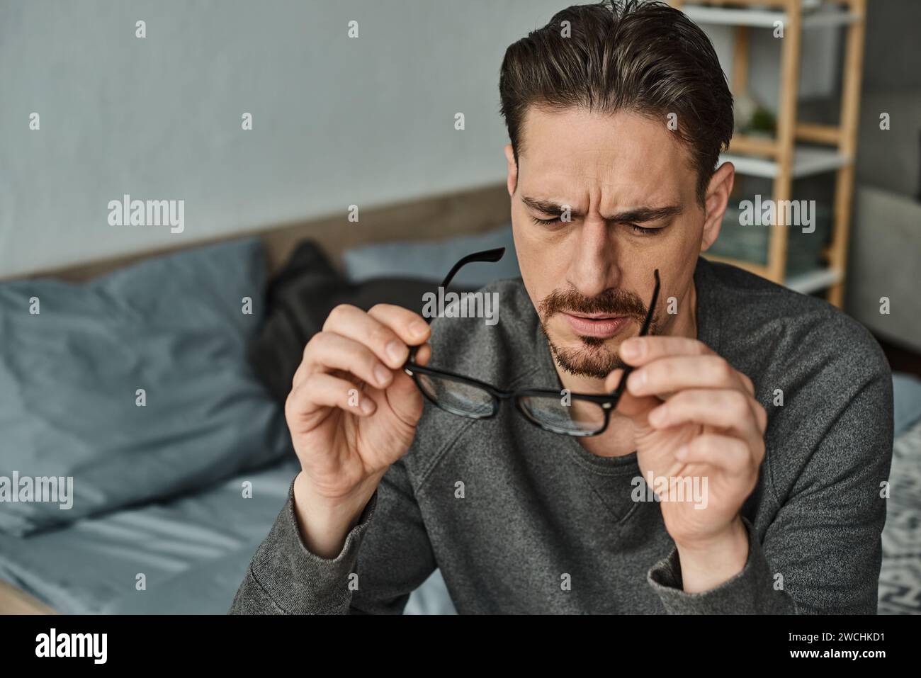 Bearded Man Frowning And Looking Carefully At His Glasses At Home