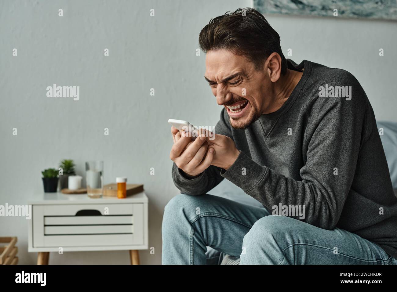 bearded man in grey jumper yelling at his smartphone while sitting on ...