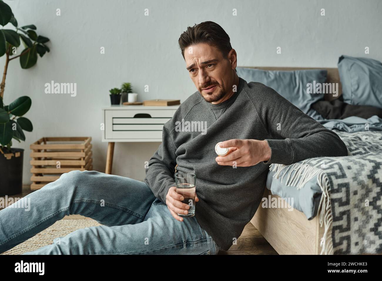 worried bearded man sitting on floor and holding glass of water and ...
