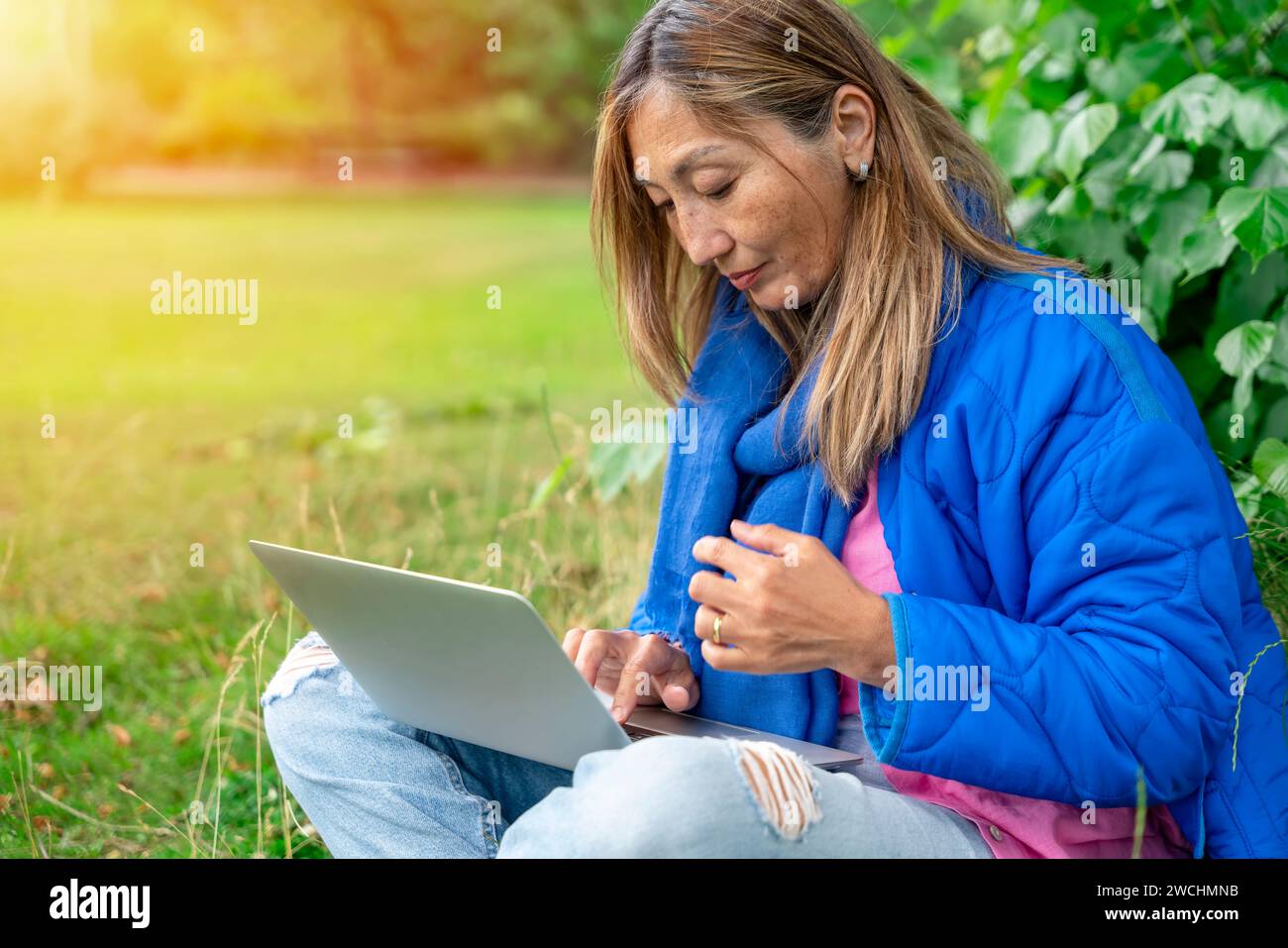 asian woman in blue jacket using laptop in public park using internet ...