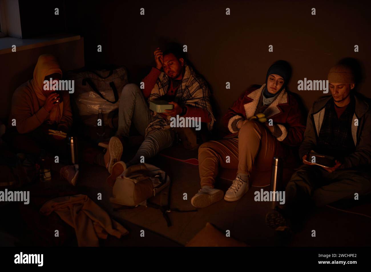 Diverse group of Middle Eastern people hiding in dark bomb shelter at ...