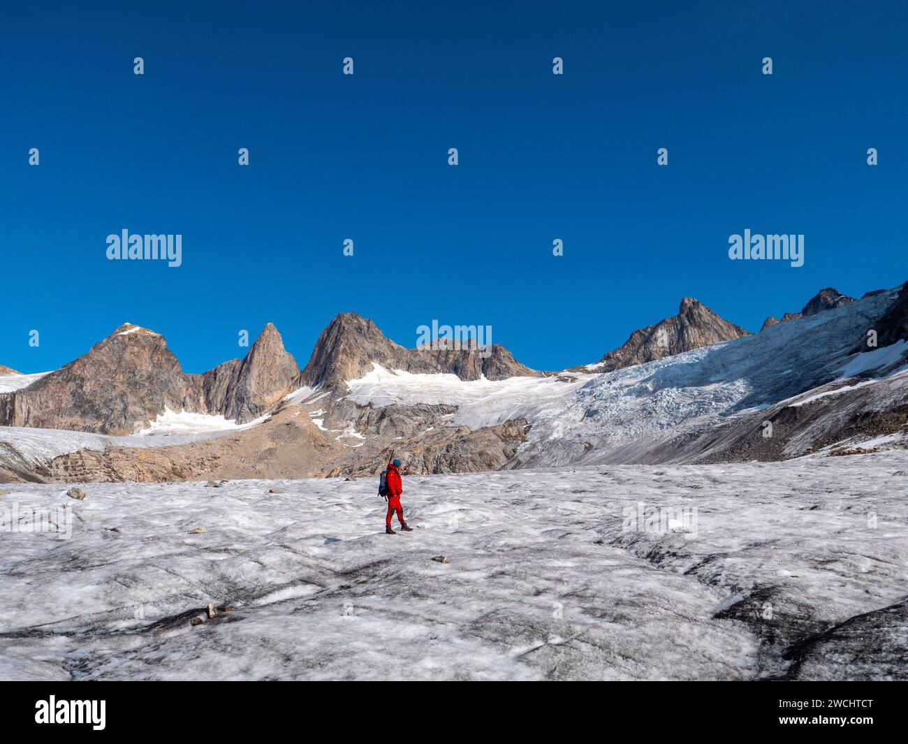 A man in red clothes stands on a glacier in front of the Niialiqaq ...