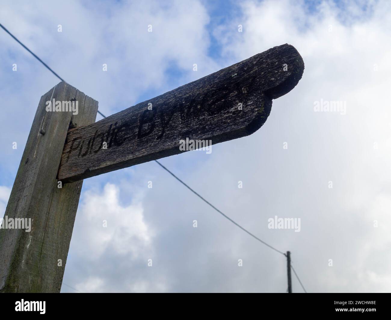 Old wooden sign pointing down a public byway, framed against a blue sky ...