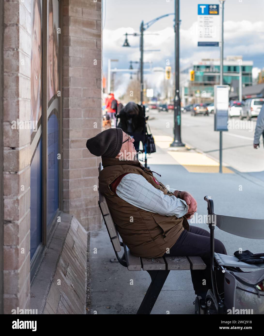 Senior man in warm clothes sits at a bus stop. Elderly Caucasian man ...