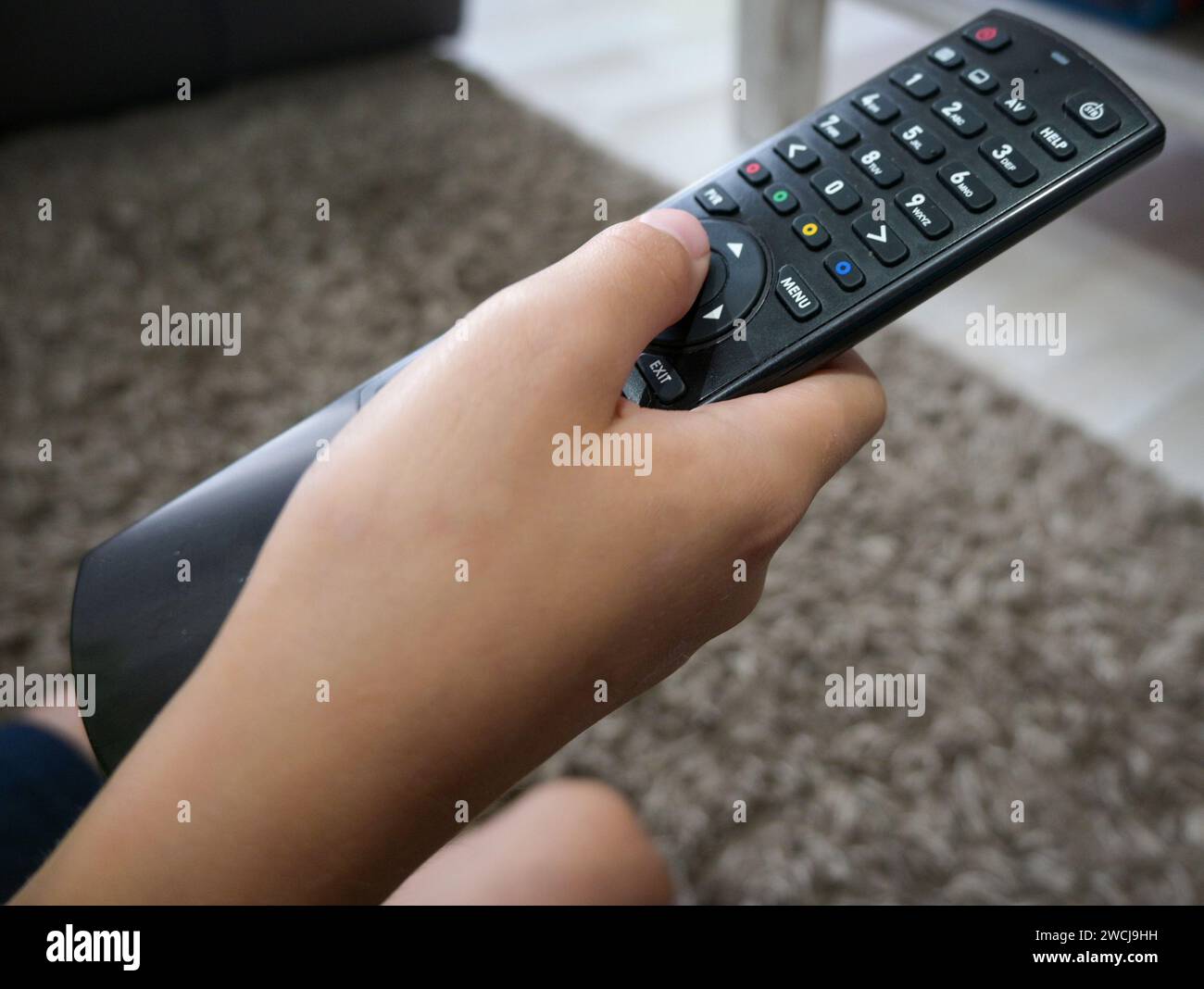 A little boy is holding a TV remote control in his hand and switching ...