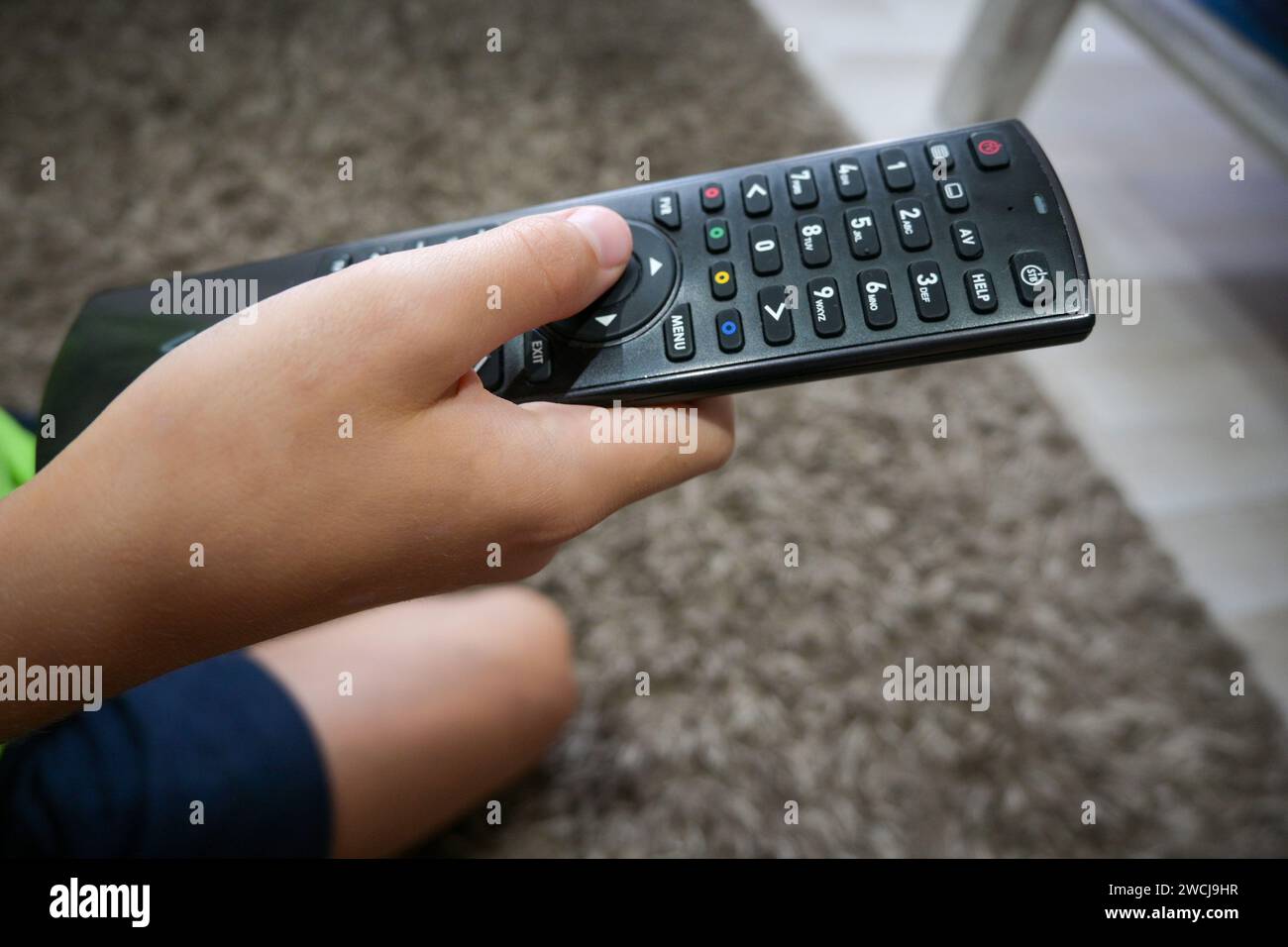 A little boy is holding a TV remote control in his hand and switching ...