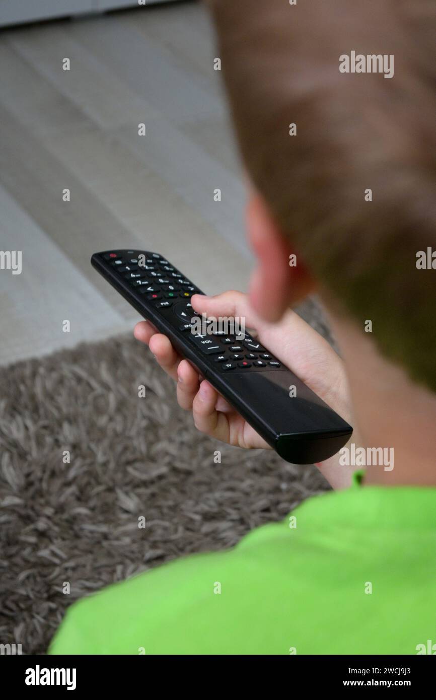 A little boy is holding a TV remote control in his hand and switching ...