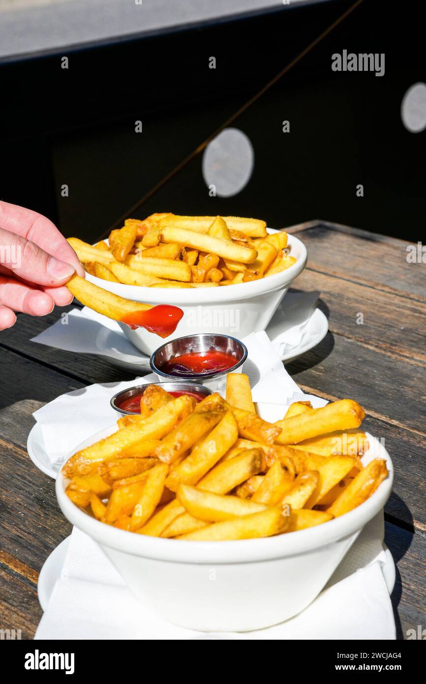 Fried fries with ketchup in a white bowl. A woman's hand holds a french ...