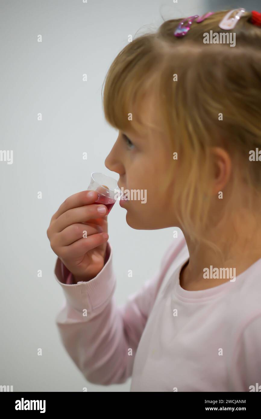 little girl in pajamas takes red cough medicine, blurred background ...