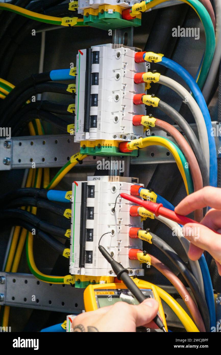 an electrician working in an electrical cabinet as Tests cables using a ...