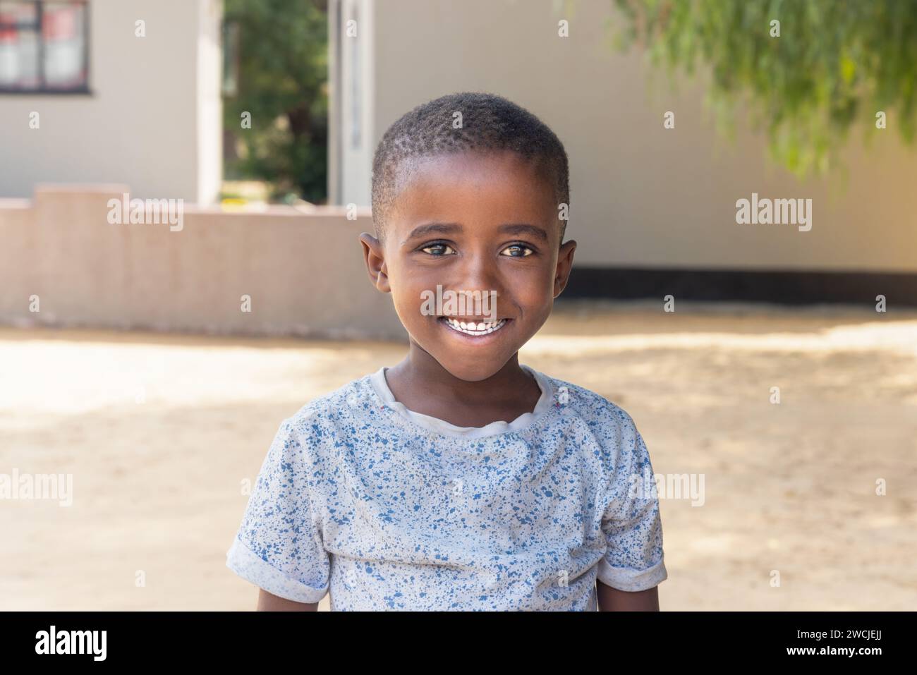 happy african kid in the village, standing in the yard, home in the ...