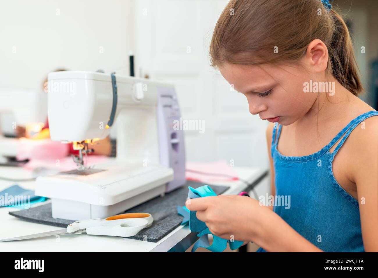 Little girl using a sewing machine to sew on a piece of fabric ...