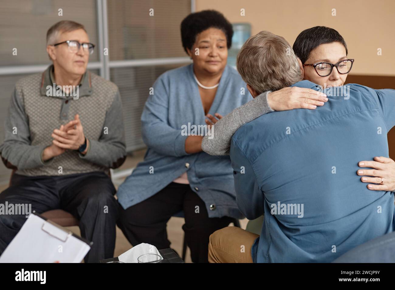 Back view of two senior people embracing in group therapy session ...