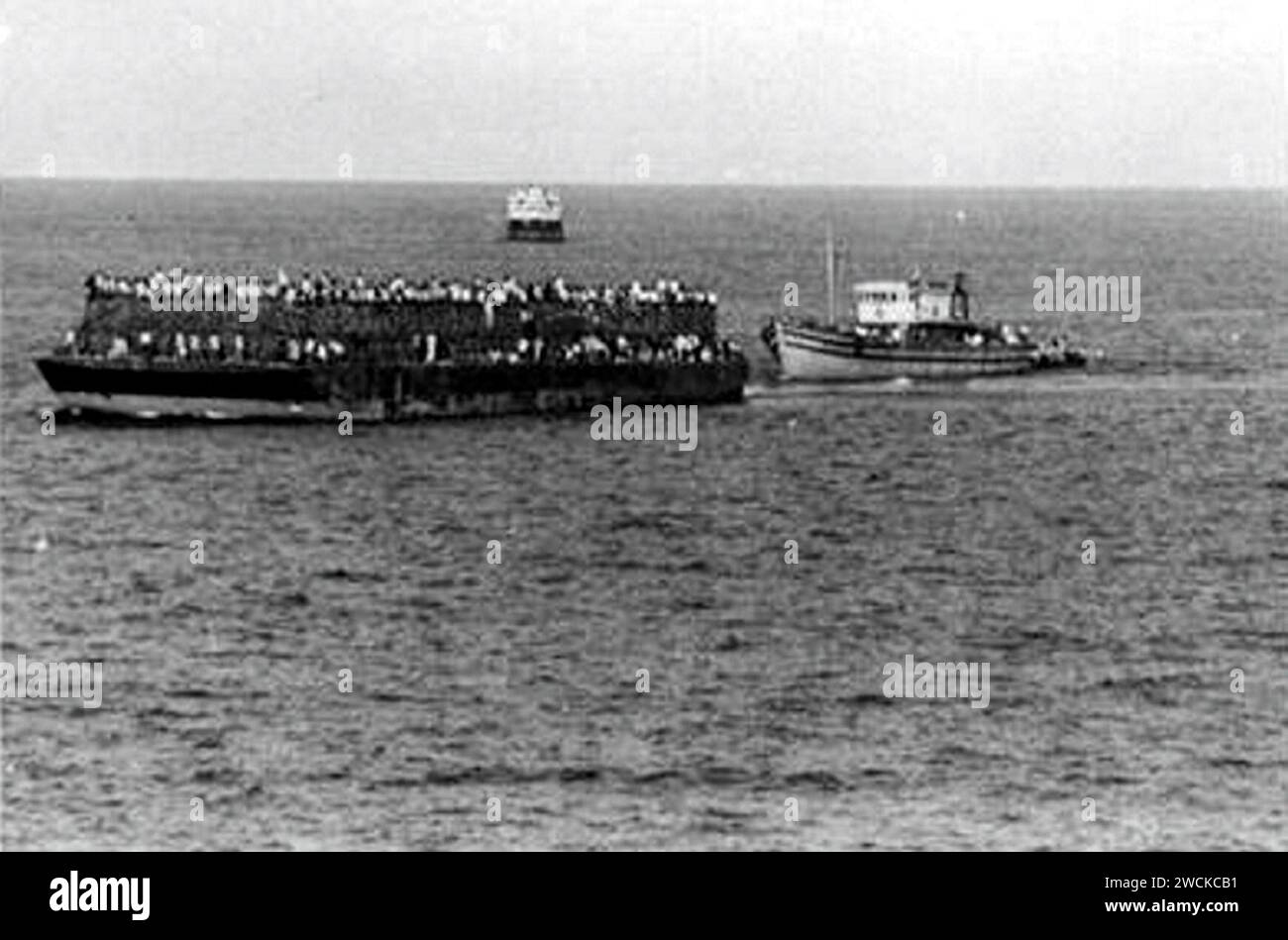 A tug pushes a barge full of Vietnamese refugees in the South China Sea ...