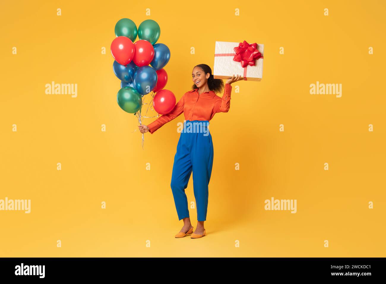 happy black teen girl holding balloons and present, yellow background ...