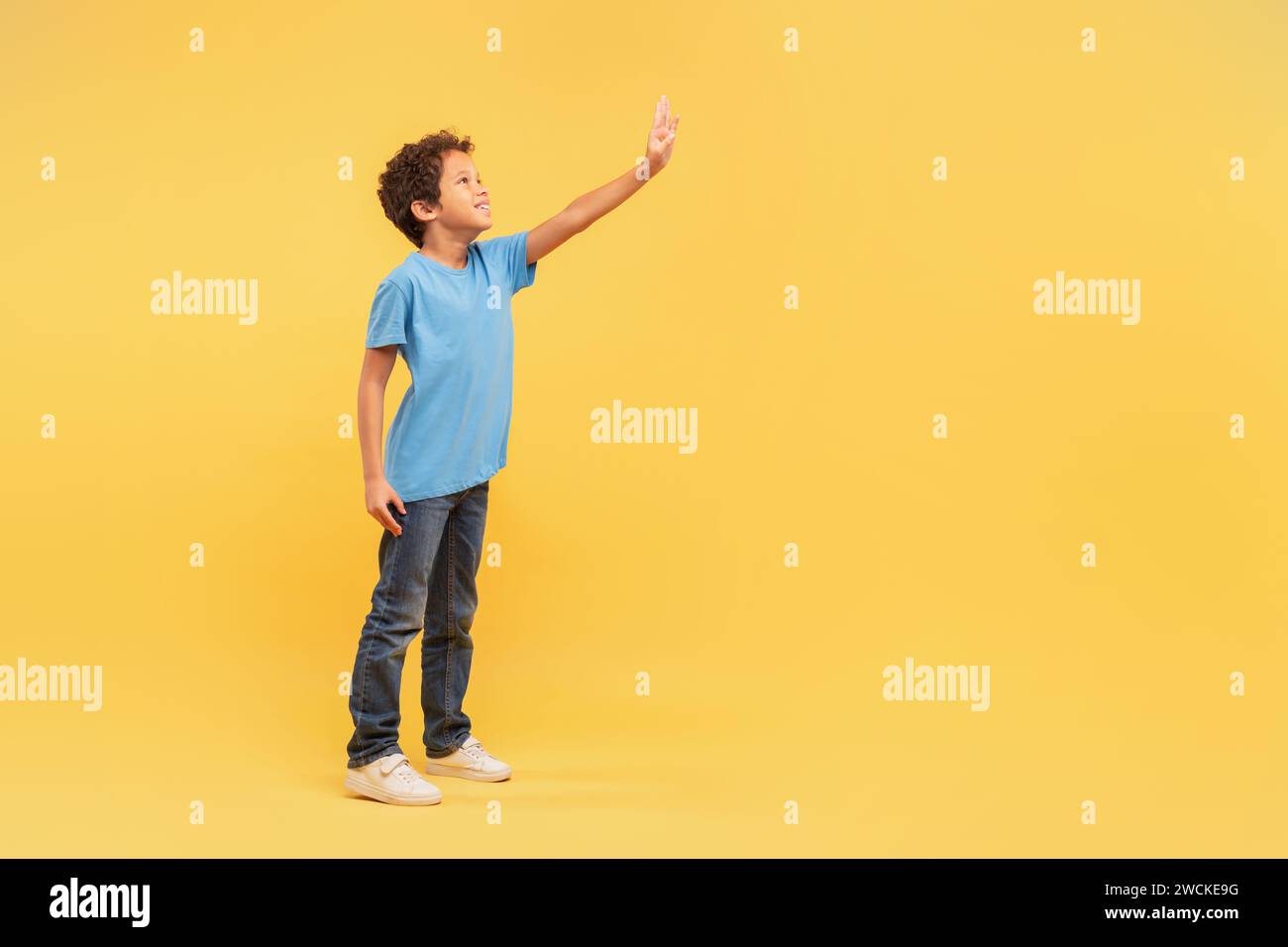 Curious boy reaching out free space in blue shirt on yellow background ...