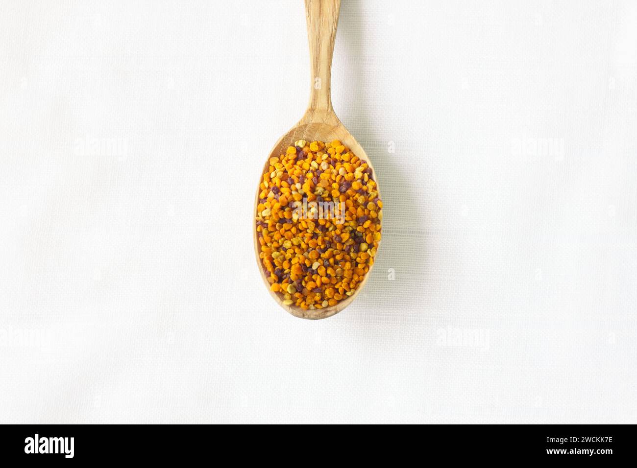 Bee pollen granules in a wooden spoon on white background. Superfood ...