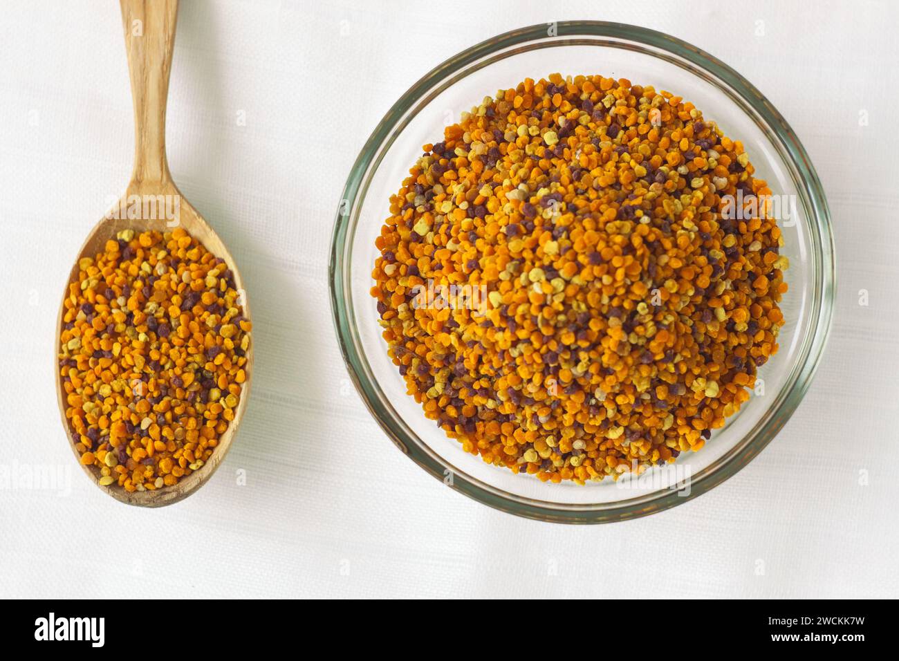 Bee pollen granules in a glass bowl and wooden spoon on white ...
