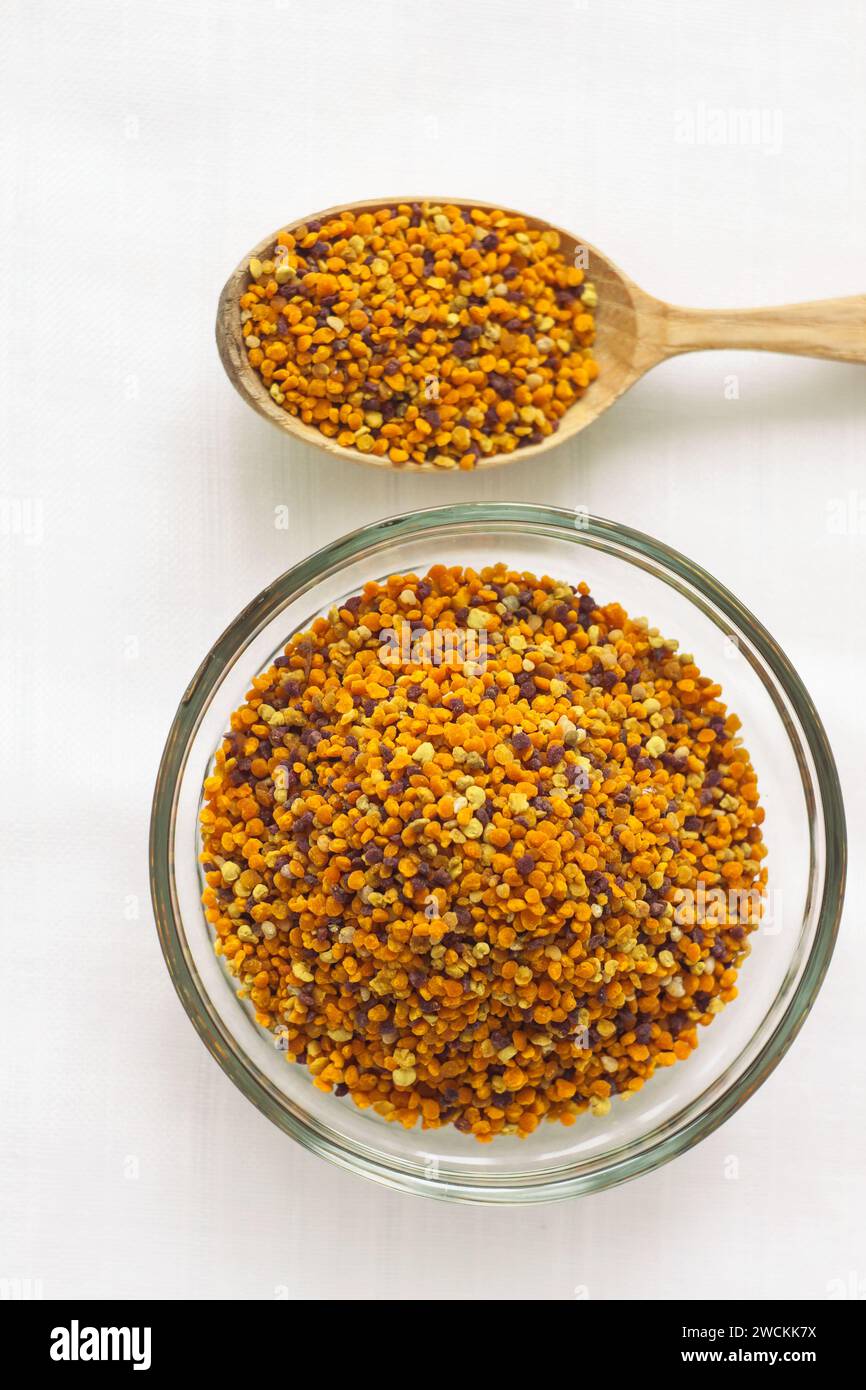 Bee pollen granules in a glass bowl and wooden spoon on white ...