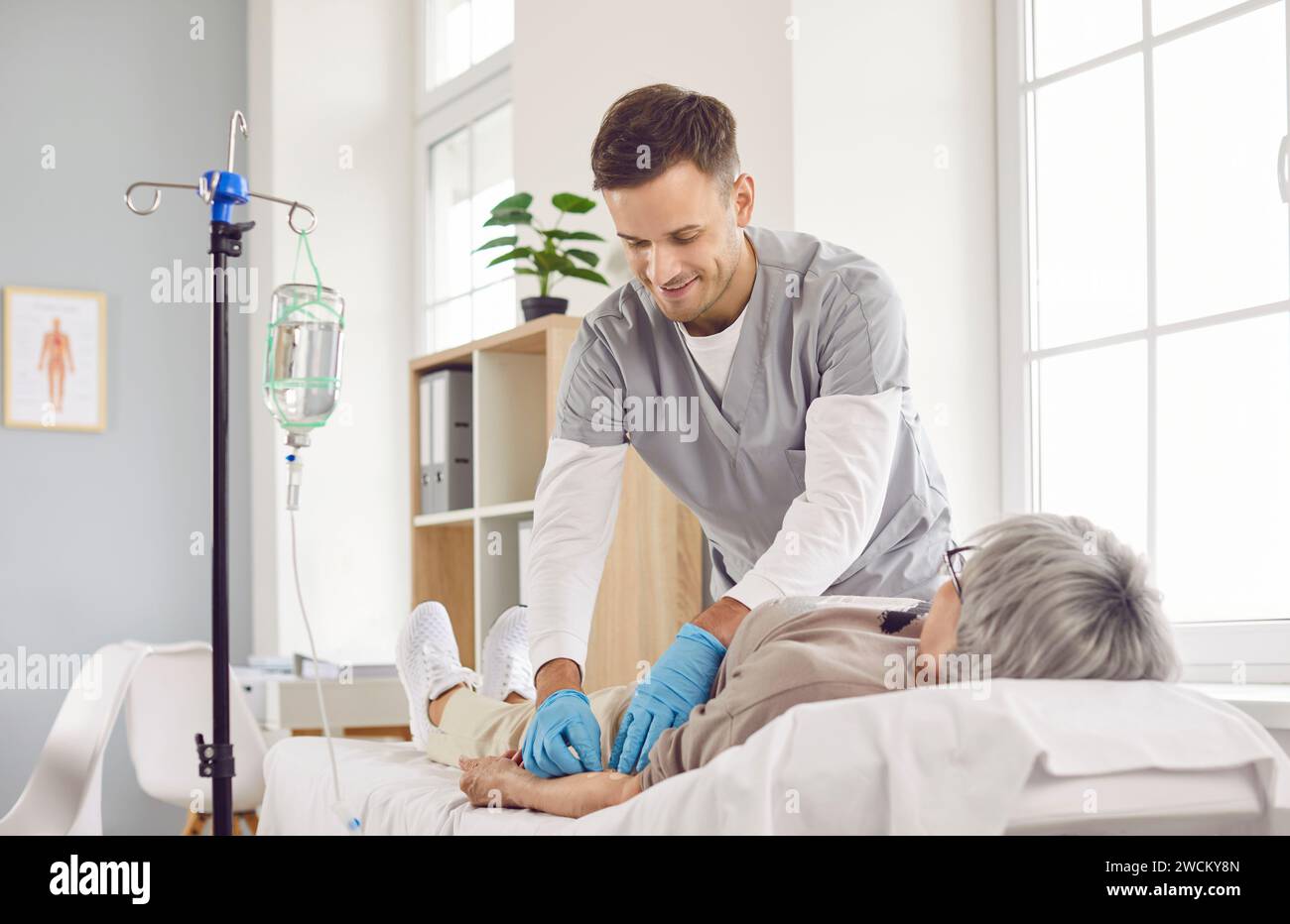 Young friendly nurse help senior patient in receiving IV drip infusion ...