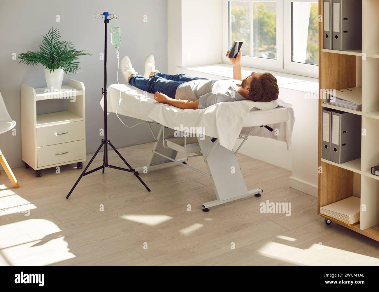 Man lying on the couch in clinic using the smartphone while receiving ...