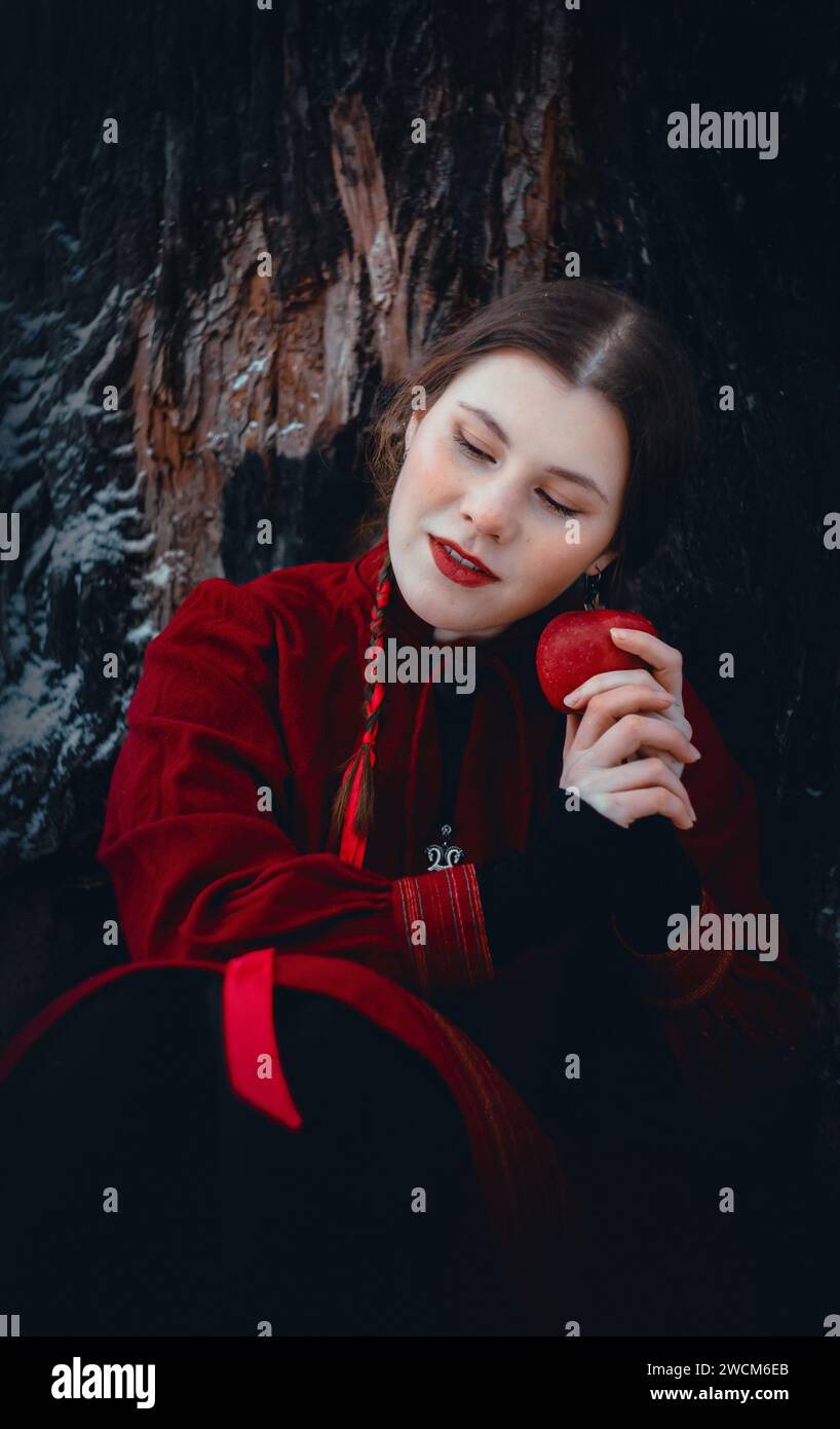 A beautiful woman in a scarlet folklore dress is sitting near a dark ...