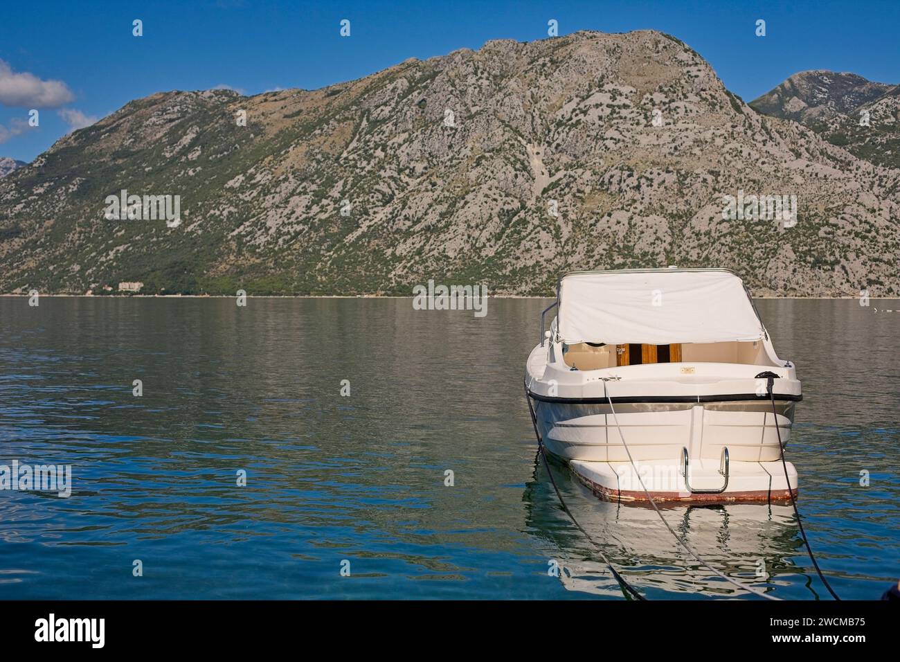 A solitary white boat floats on the calm waters of Kotor Bay, the ...