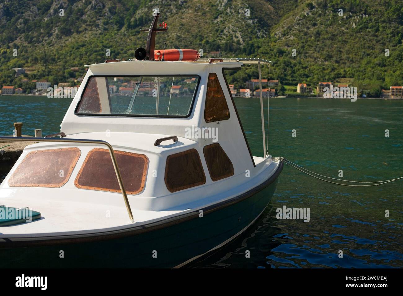 A solitary white boat floats on the calm waters of Kotor Bay, the ...